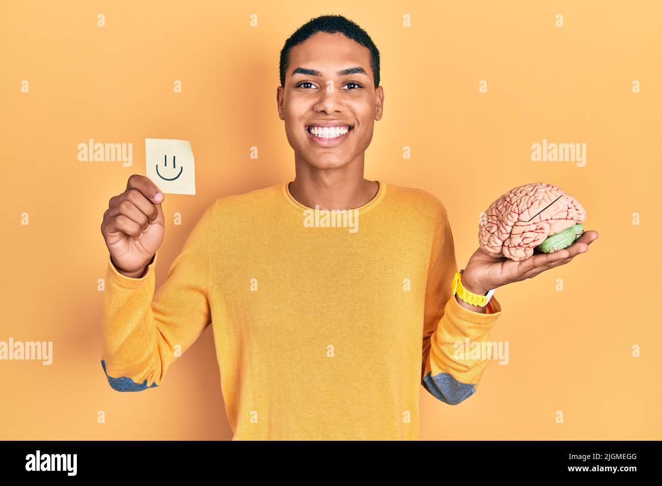 Young african american guy holding smile reminder and brain smiling ...