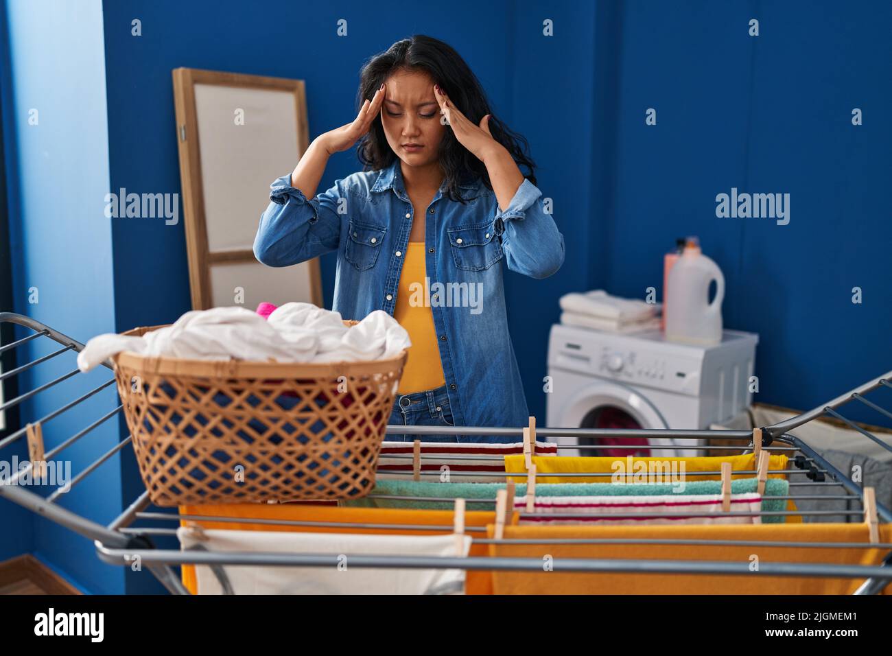 Young asian woman hanging clothes at clothesline with hand on head for ...