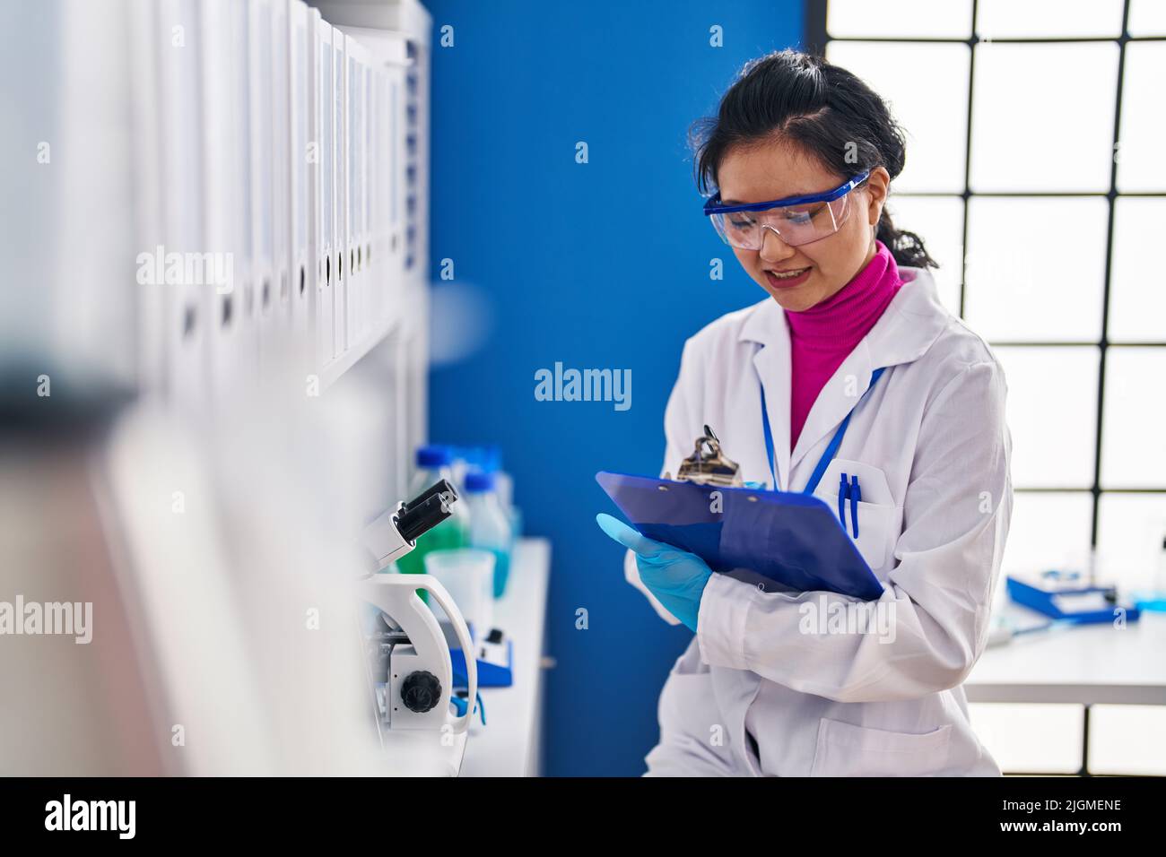 Young chinese woman scientist smiling confident write on clipboard at ...