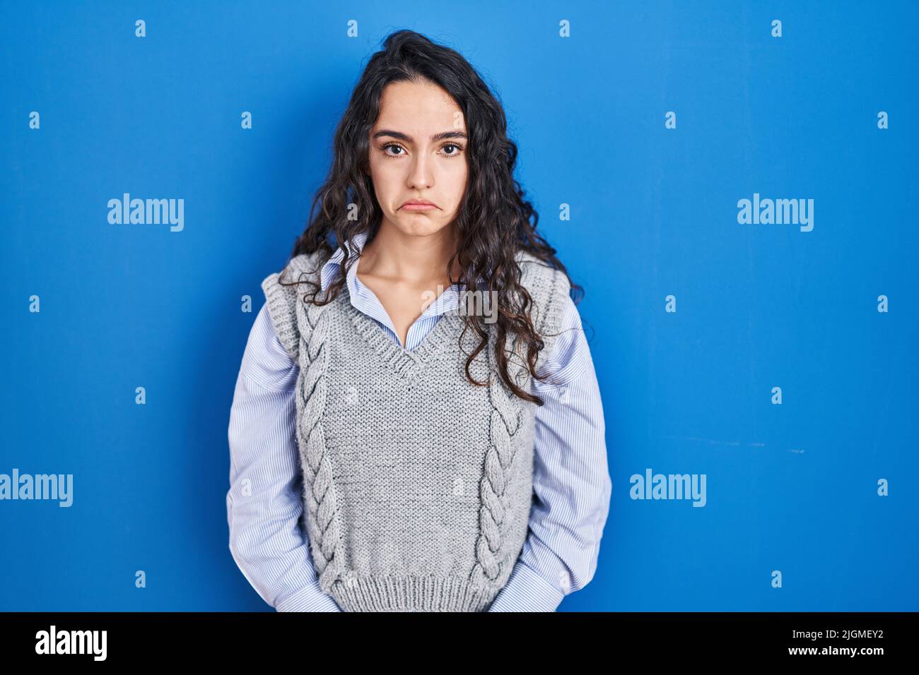Young brunette woman standing over blue background depressed and worry ...