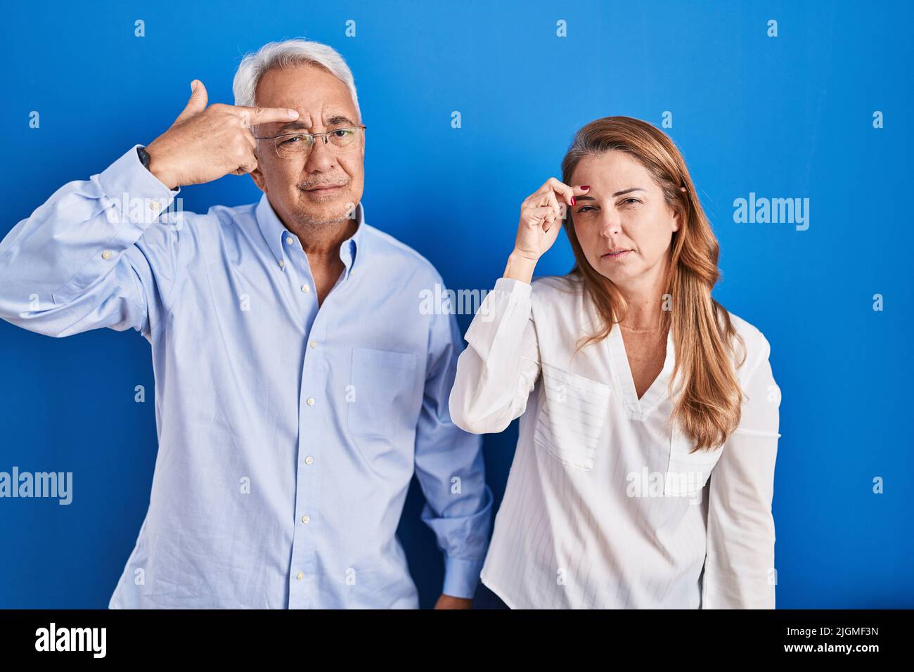 Middle age hispanic couple standing over blue background pointing ...