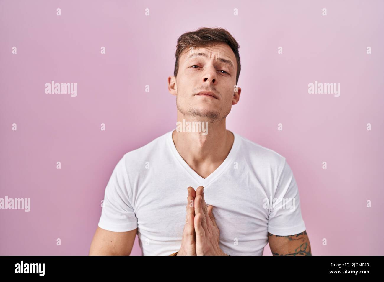 Caucasian man standing over pink background begging and praying with ...