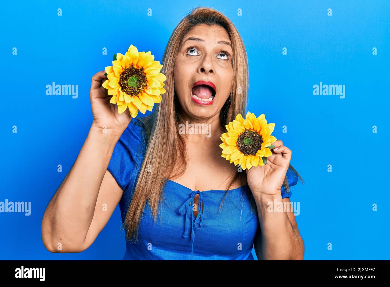 Middle age hispanic woman holding yellow sunflowers angry and mad ...