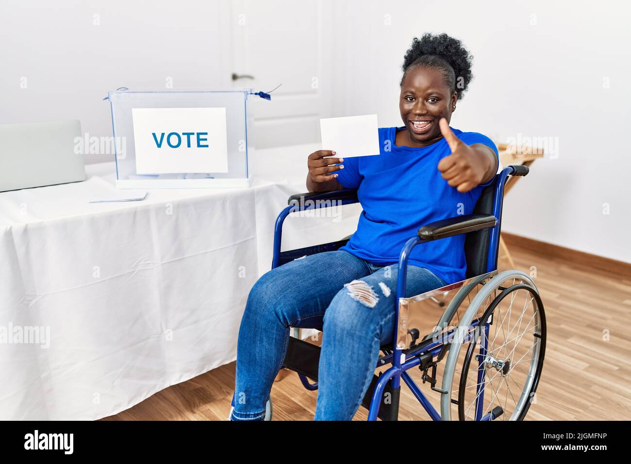 Young african woman sitting on wheelchair voting putting envelop in ...