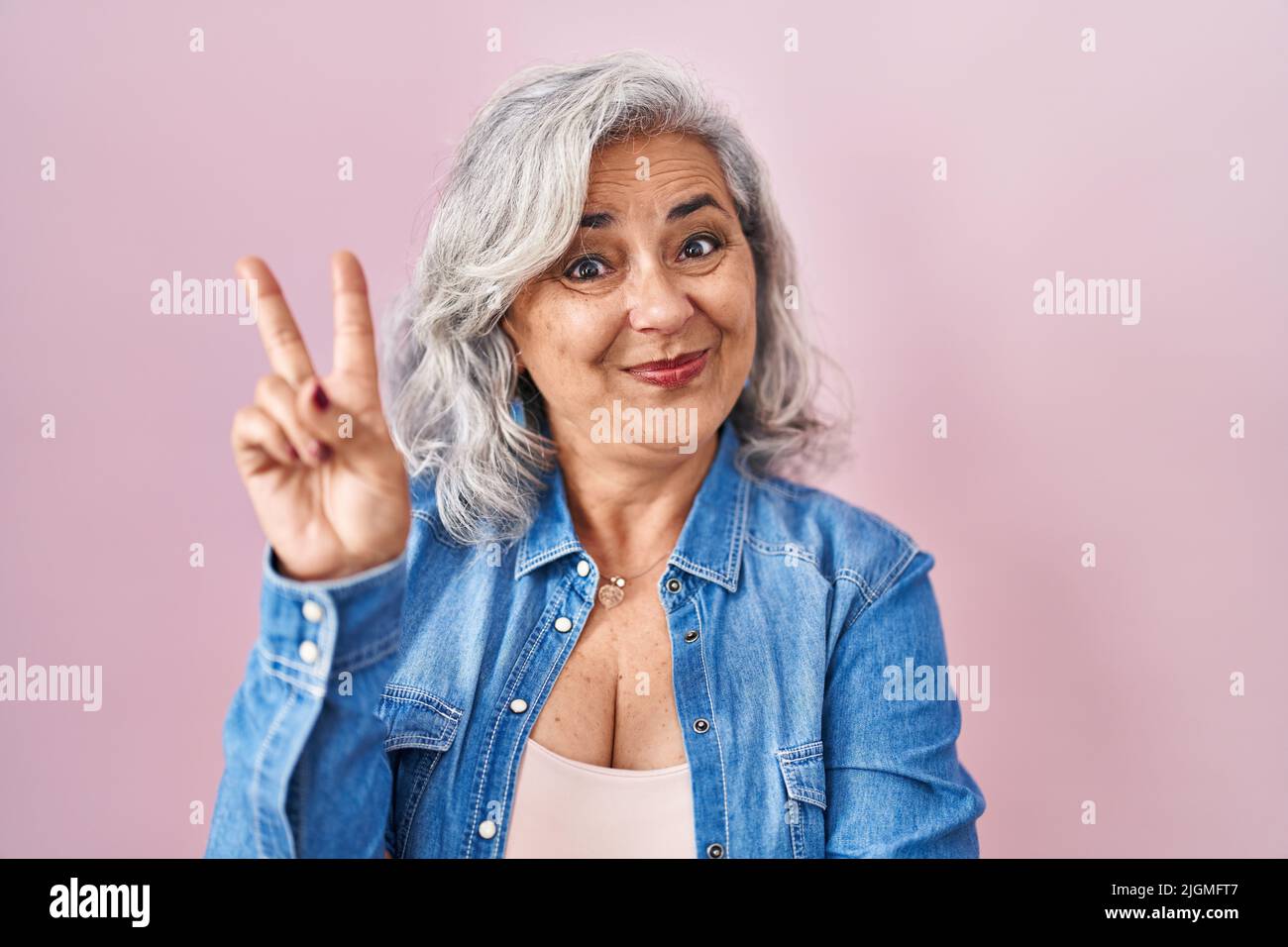 Middle age woman with grey hair standing over pink background smiling ...