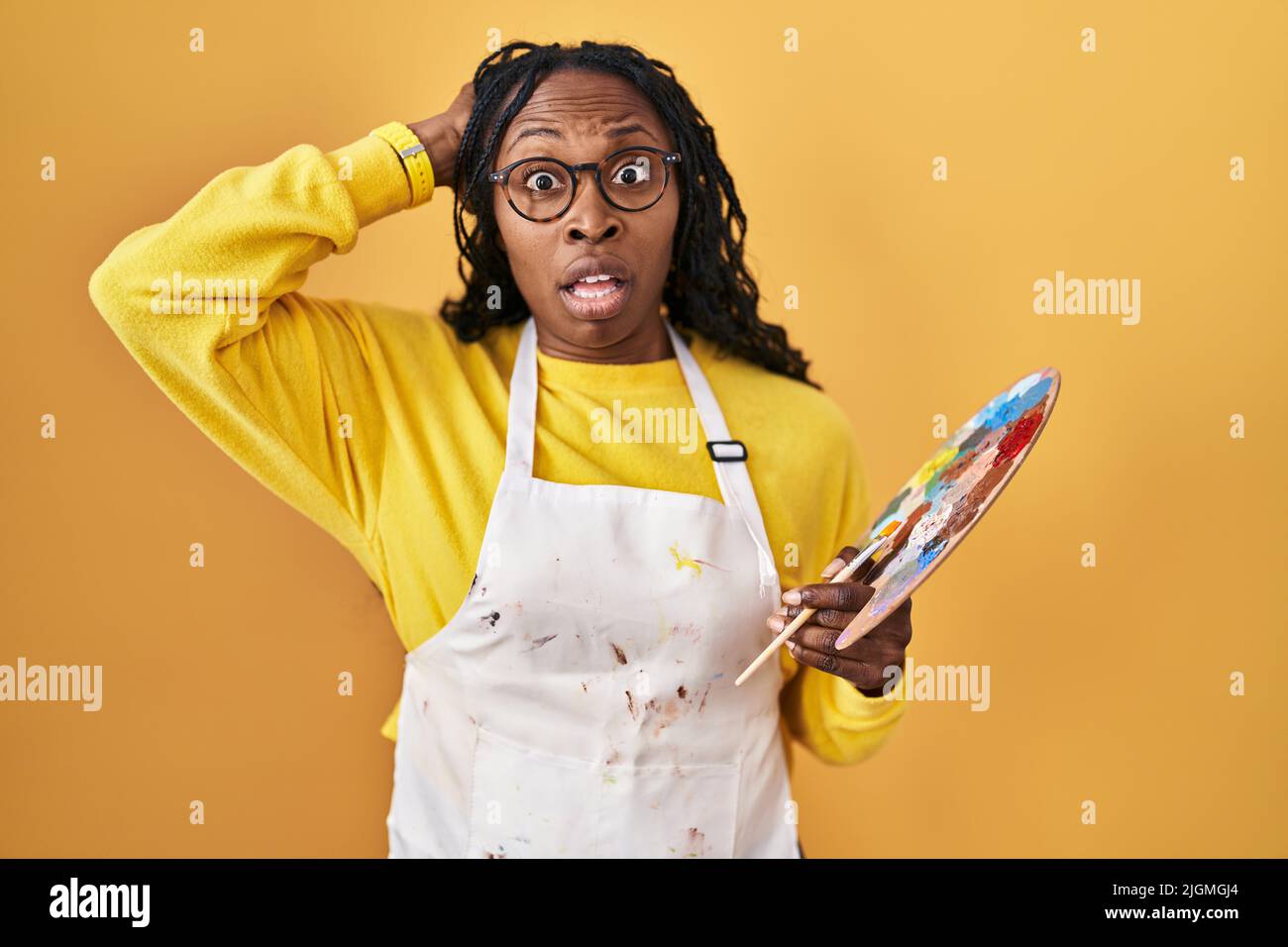 African woman holding painter palette crazy and scared with hands on ...