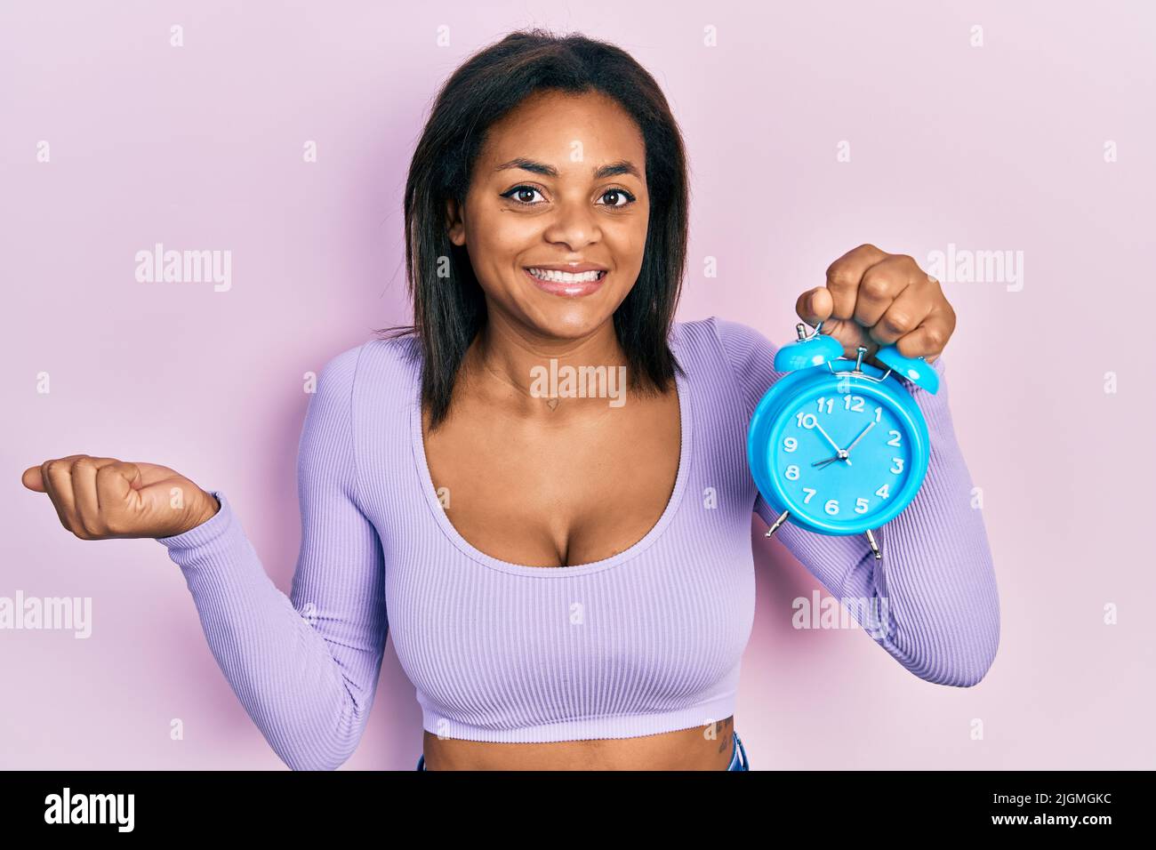 Young african american girl holding alarm clock screaming proud ...