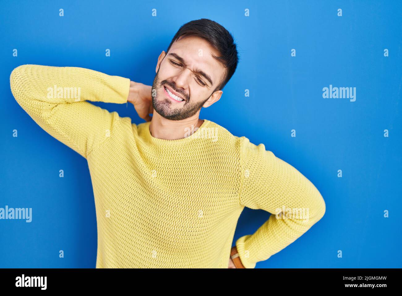 Hispanic man standing over blue background suffering of neck ache ...