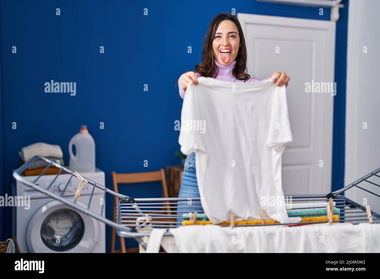 Young brunette woman hanging clothes at clothesline sticking tongue out ...