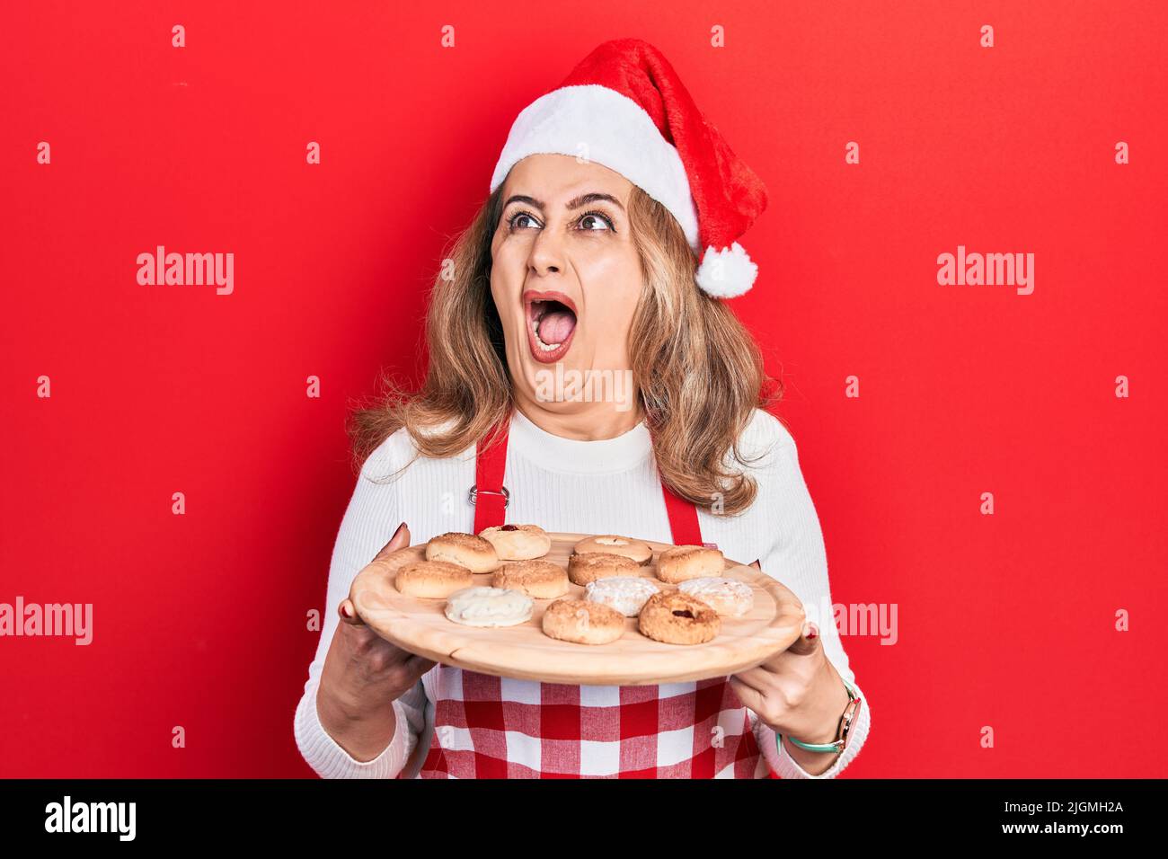 Middle age caucasian woman wearing baker apron and christmas hat ...
