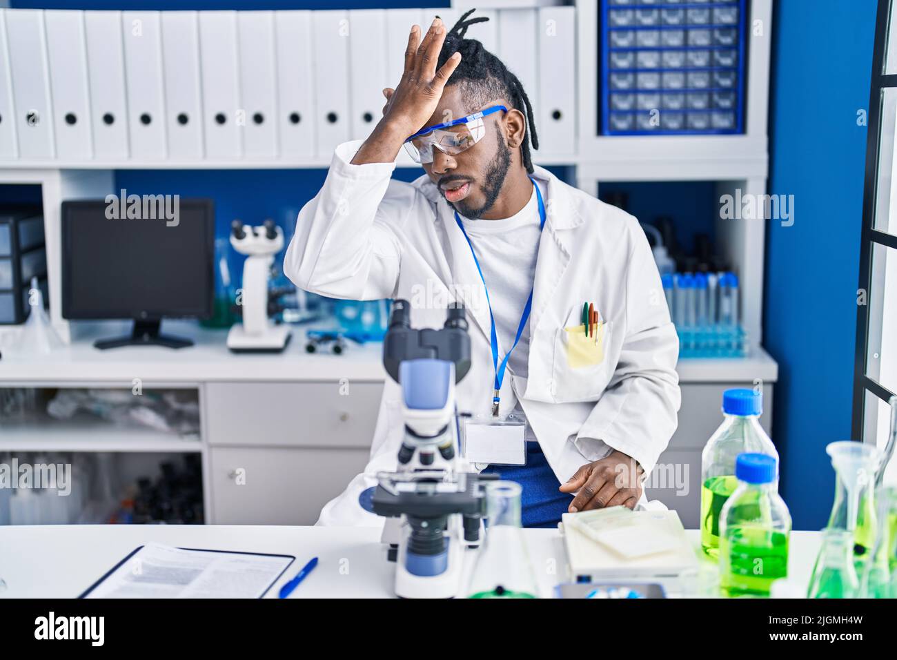 African man with dreadlocks working at scientist laboratory surprised with hand on head for ...