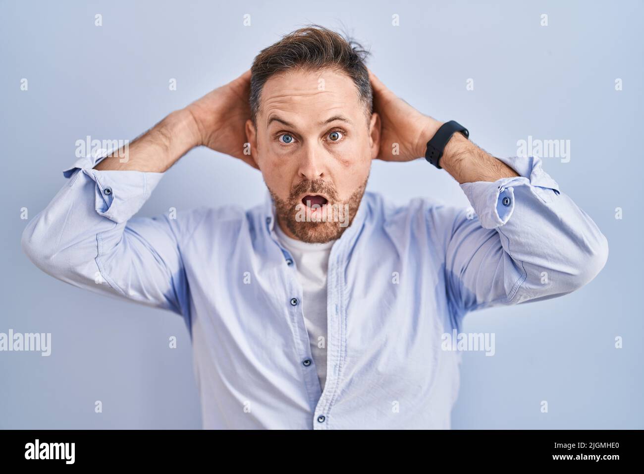 Middle age caucasian man standing over blue background crazy and scared ...