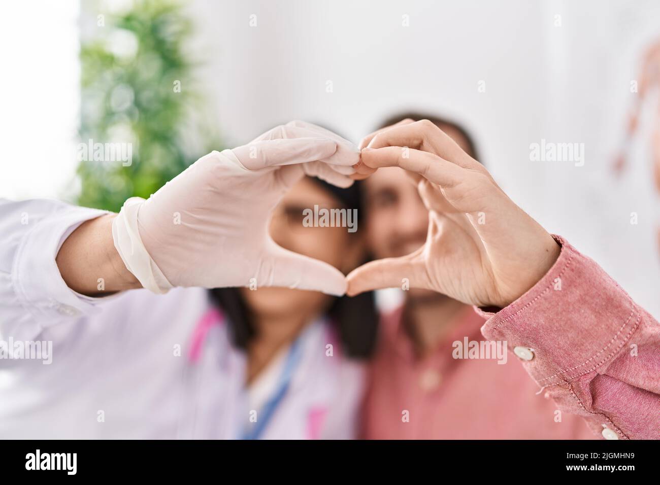 Man and woman doctor and patient doing heart gesture with hands at ...