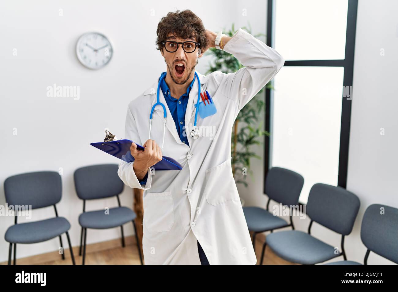 Young hispanic doctor man at waiting room crazy and scared with hands ...