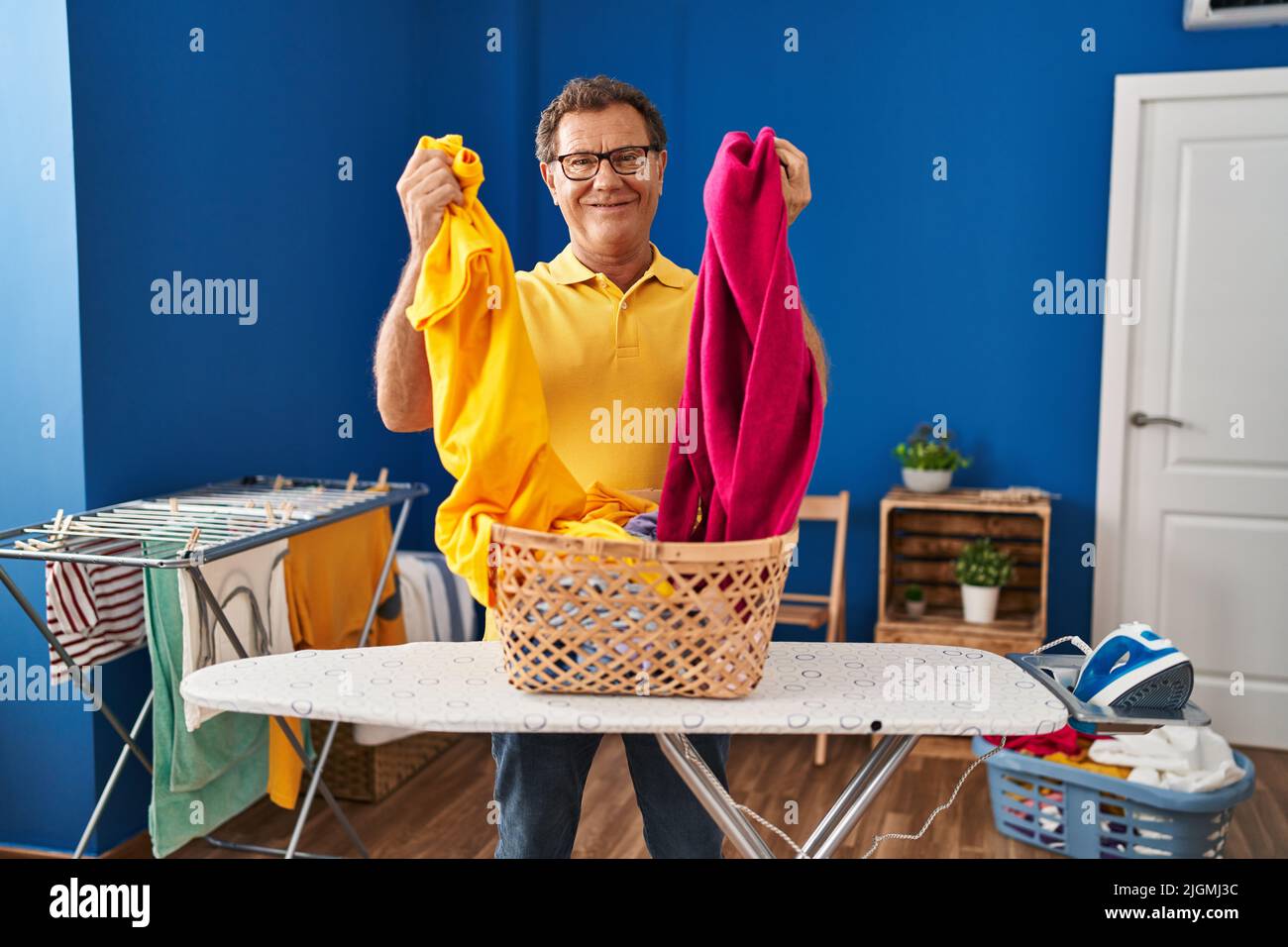 Middle age man smiling confident holding clothes of basket at laundry ...