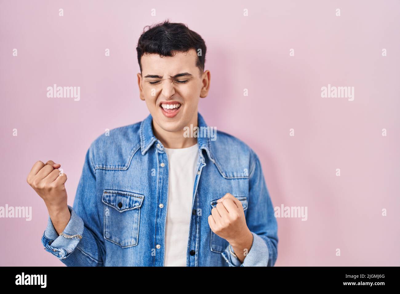 Non binary person standing over pink background very happy and excited ...