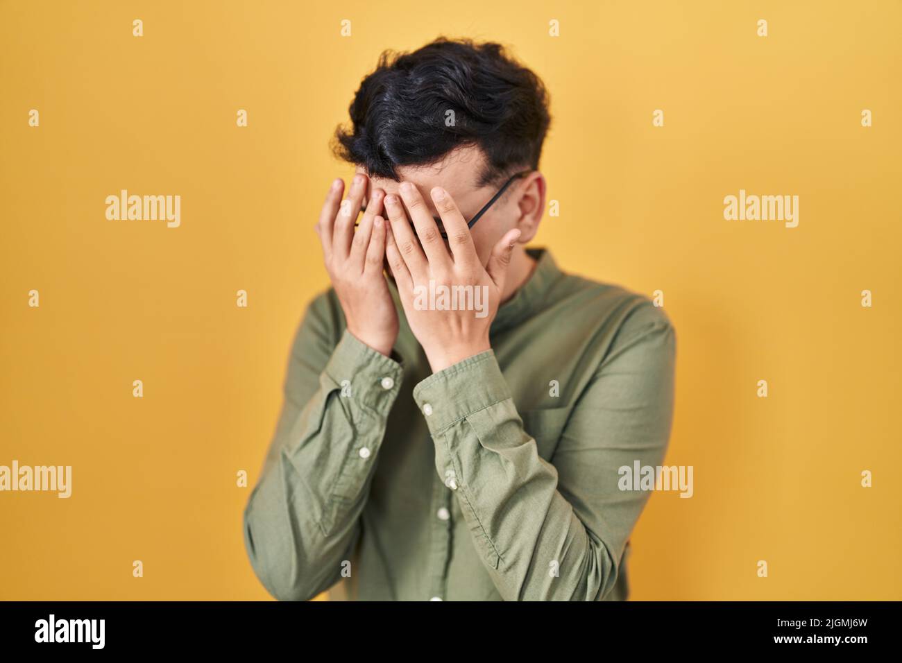 Non binary person standing over yellow background with sad expression ...