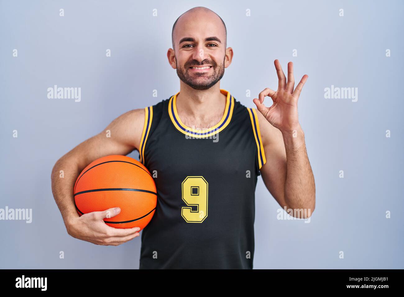 Young bald man with beard wearing basketball uniform holding ball ...