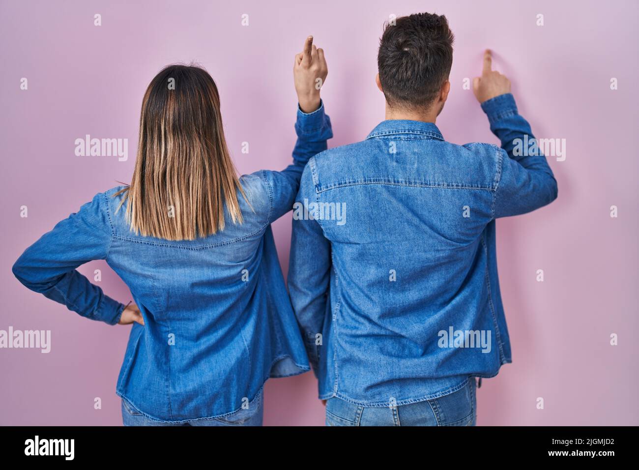 Young hispanic couple standing over pink background posing backwards ...