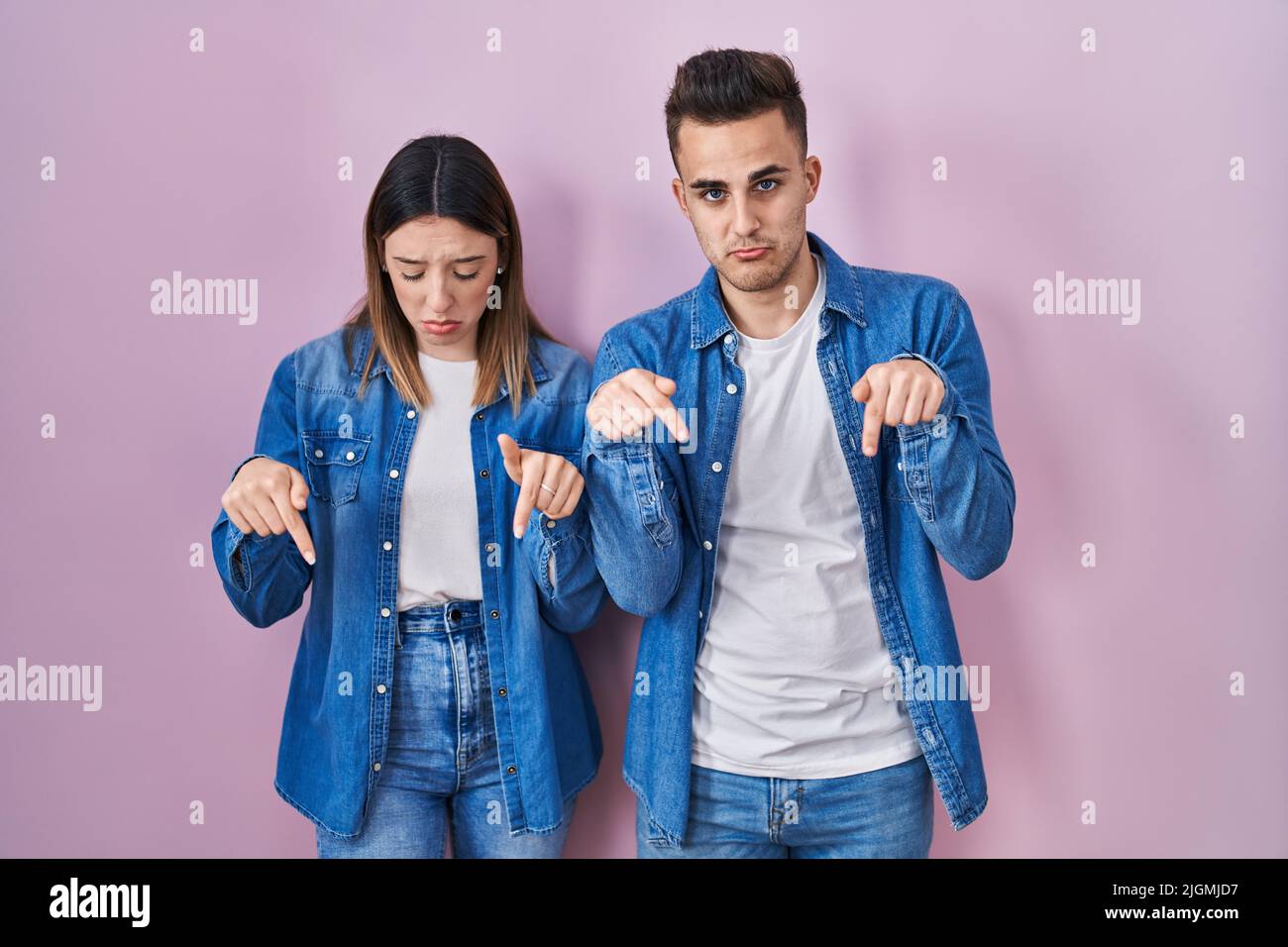 Young hispanic couple standing over pink background pointing down ...