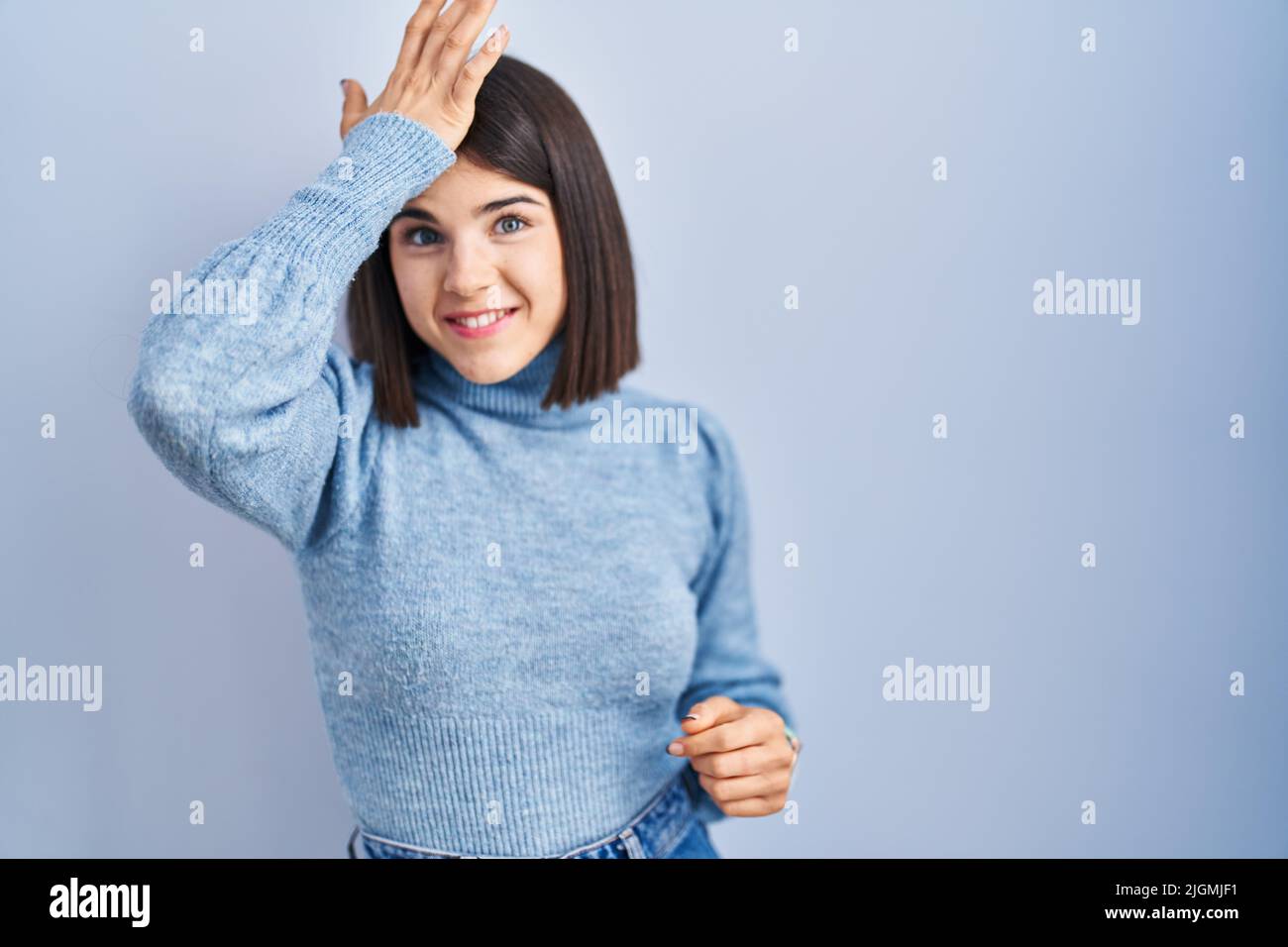 Young hispanic woman standing over blue background surprised with hand ...