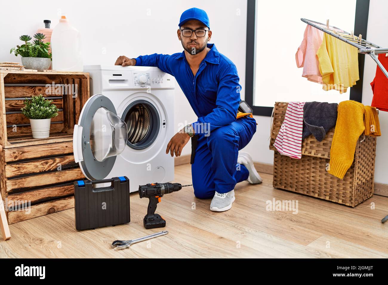 Young indian technician working on washing machine puffing cheeks with ...