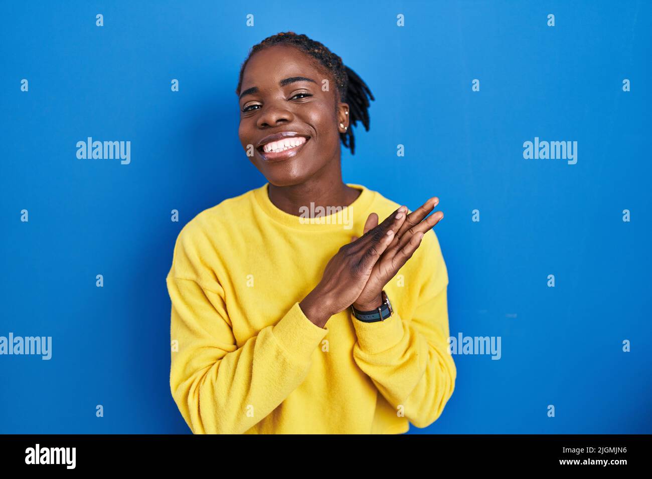 Beautiful black woman standing over blue background clapping and ...