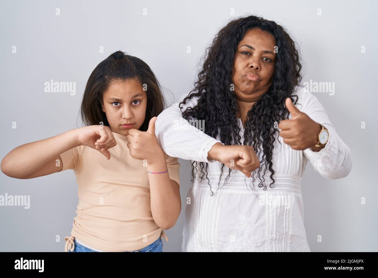 Mother and young daughter standing over white background doing thumbs ...