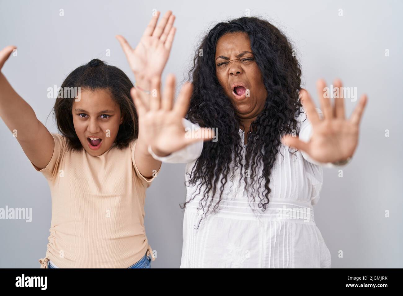 Mother and young daughter standing over white background doing stop ...