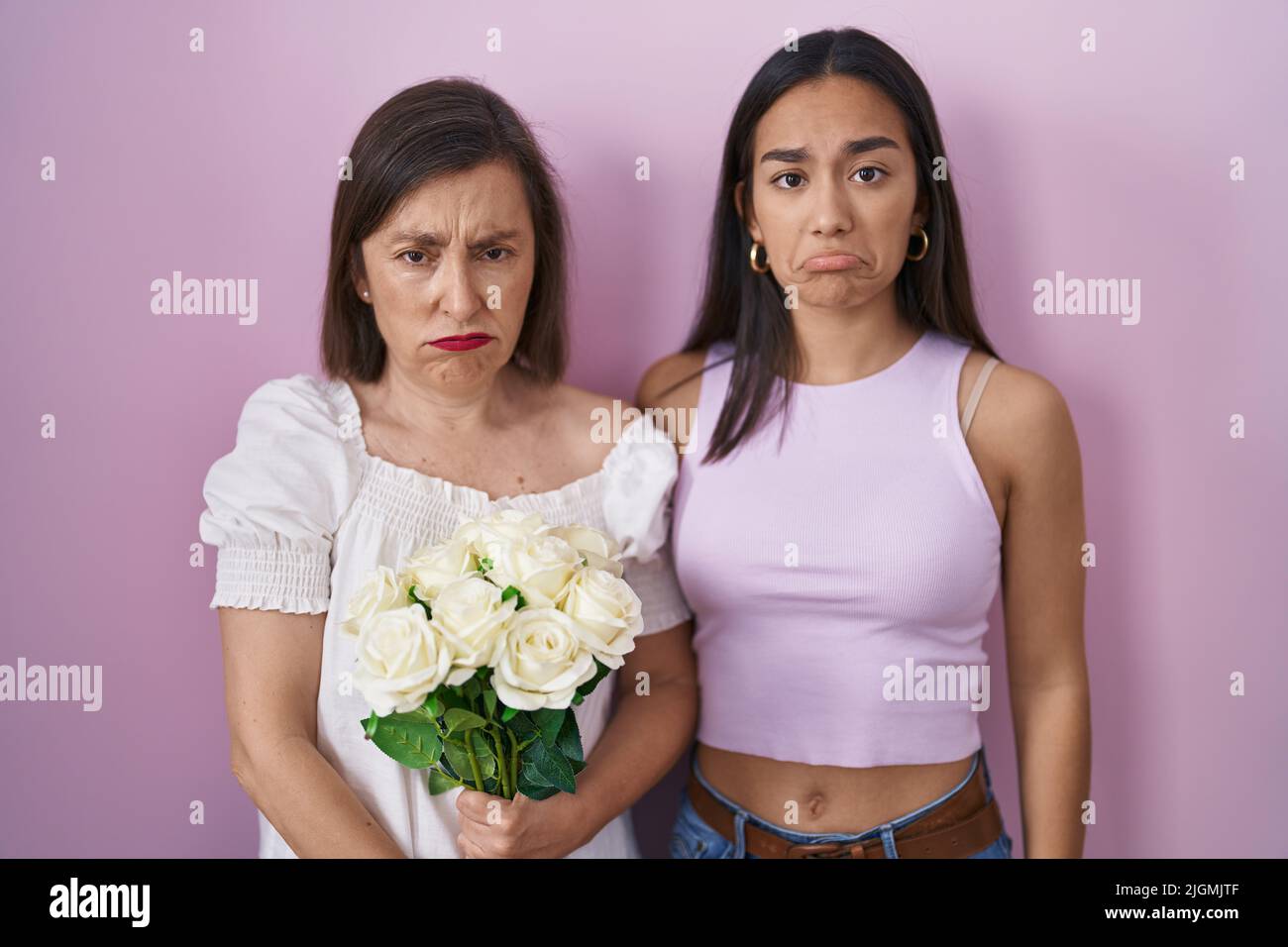 Hispanic mother and daughter holding bouquet of white flowers depressed ...