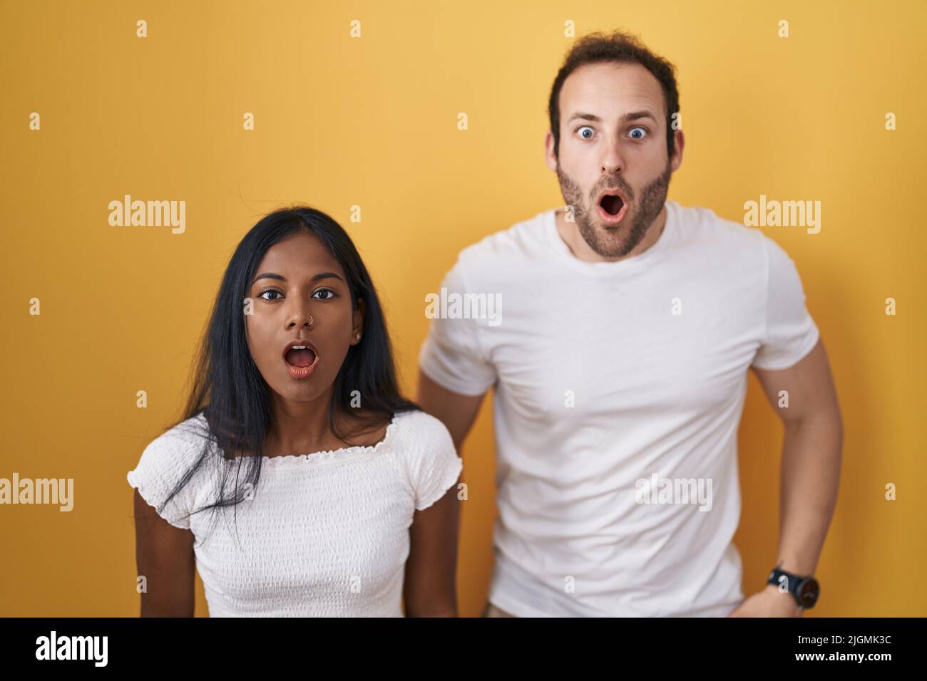 Interracial couple standing over yellow background afraid and shocked ...