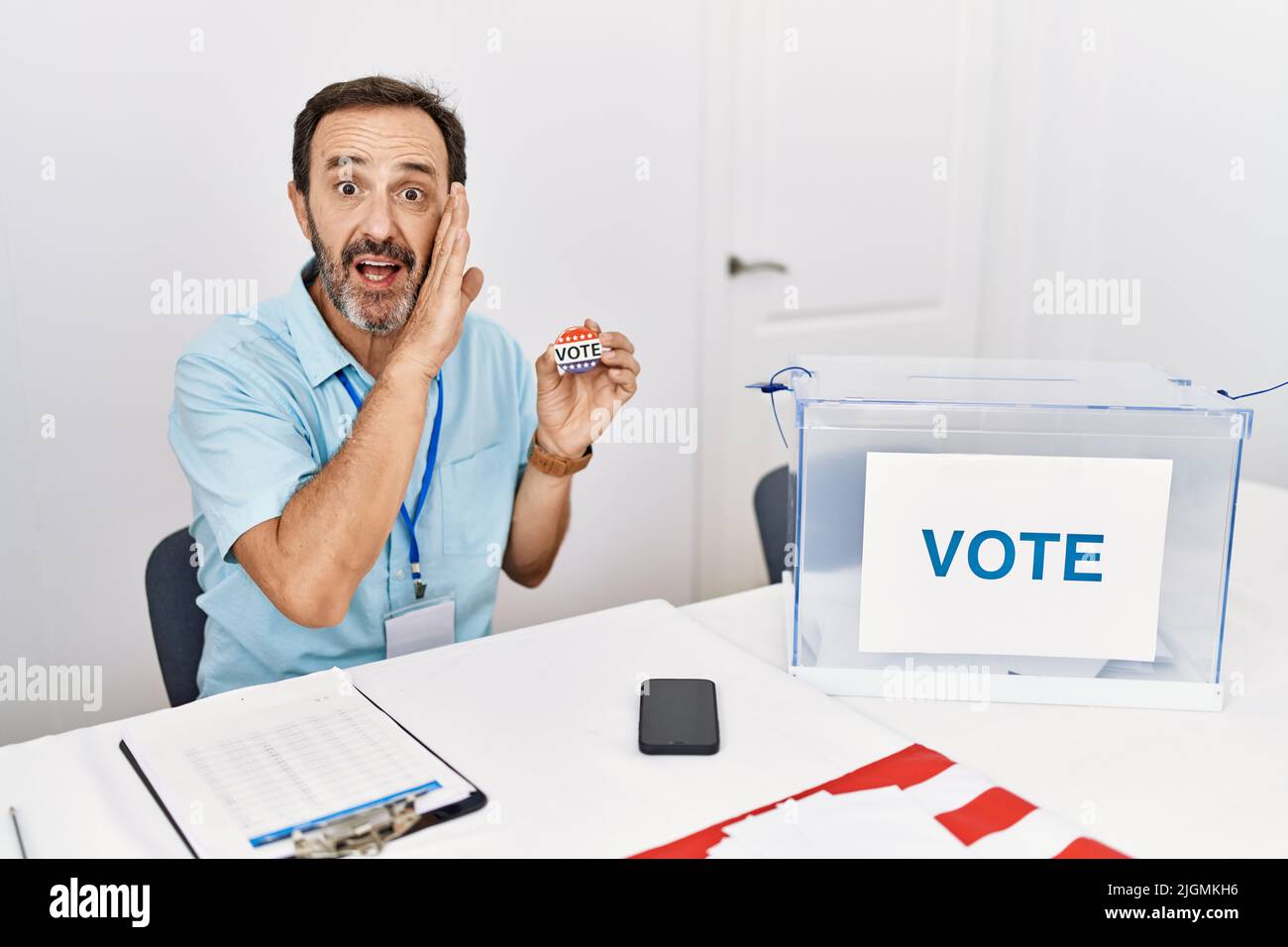 Middle age man with beard sitting by ballot holding i vote badge hand ...