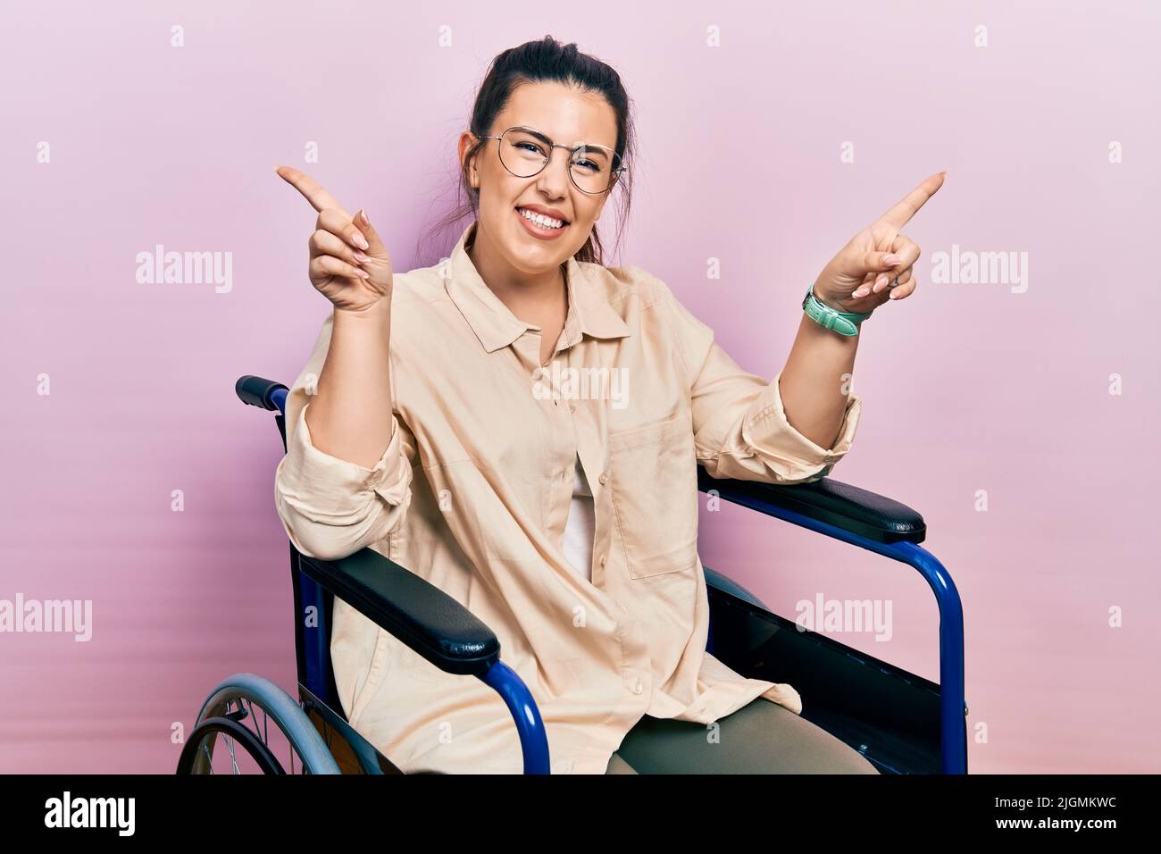 Young hispanic woman sitting on wheelchair smiling confident pointing ...