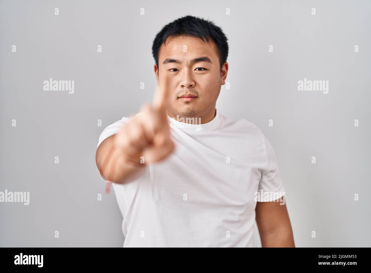 Young chinese man standing over white background pointing with finger ...