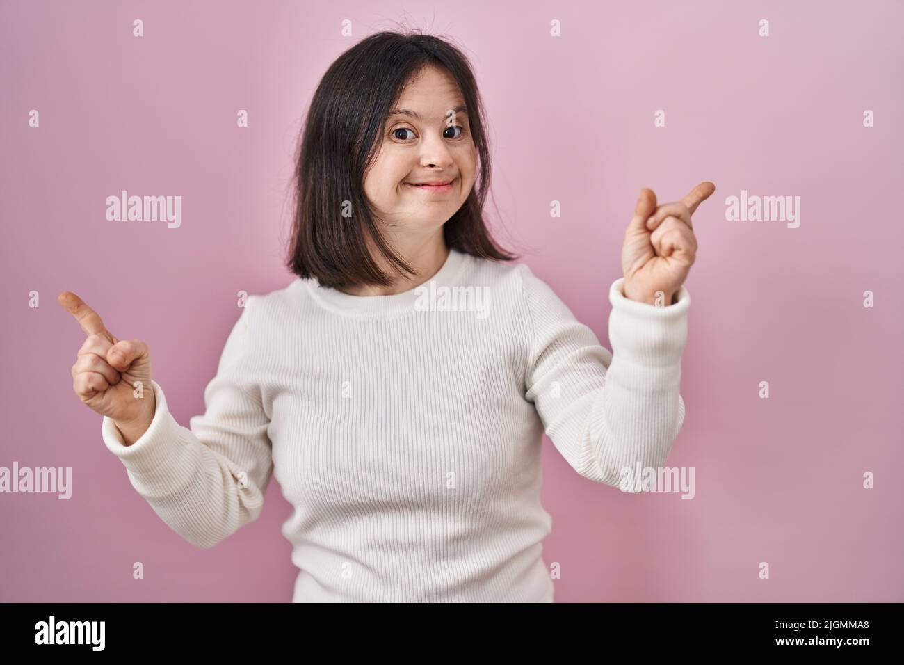 Woman with down syndrome standing over pink background smiling ...