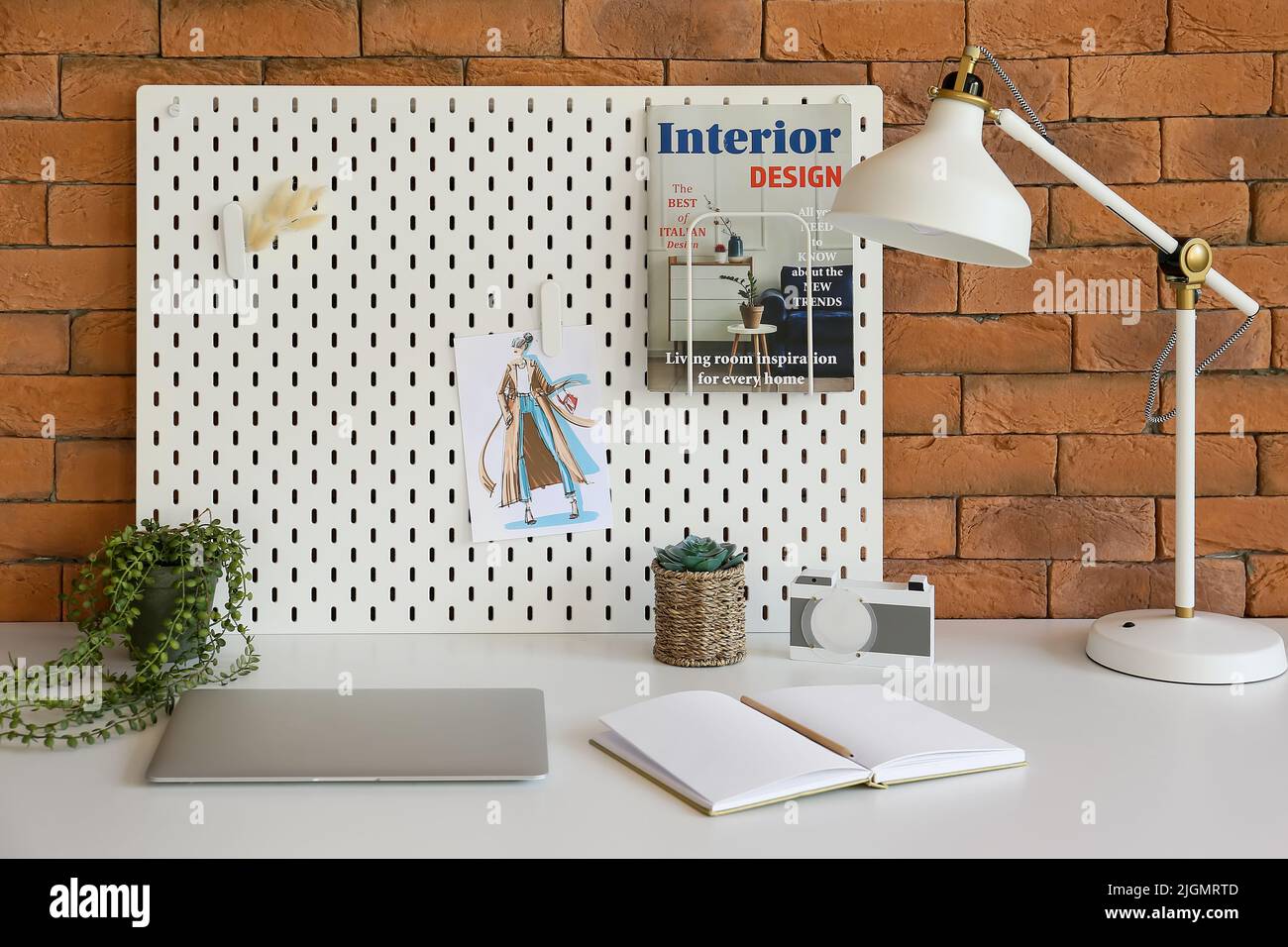 Modern workplace with peg board, laptop and lamp near brick wall Stock ...