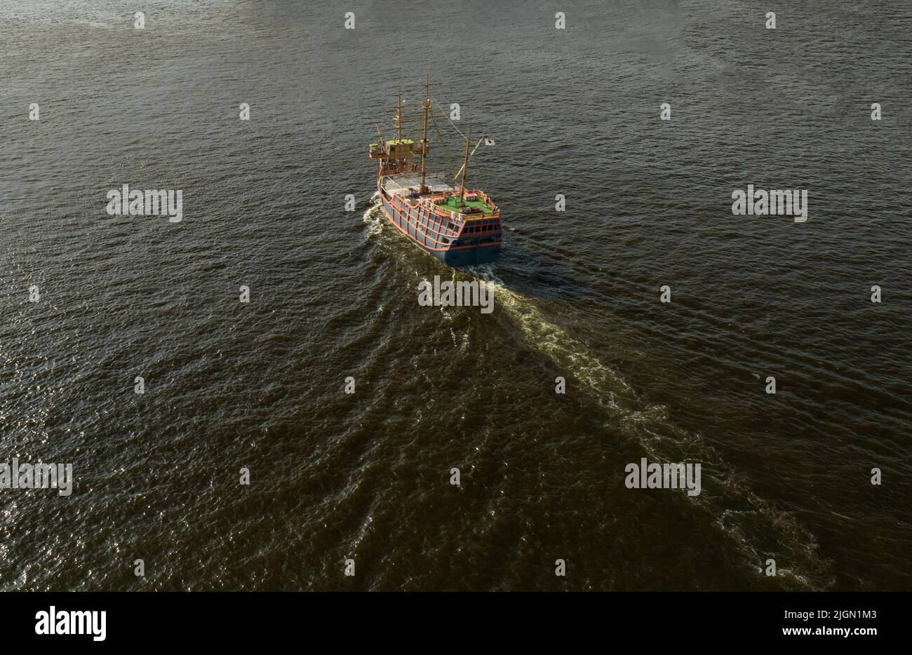 Old style pirate ship motoring without sails in open water towards sun ...