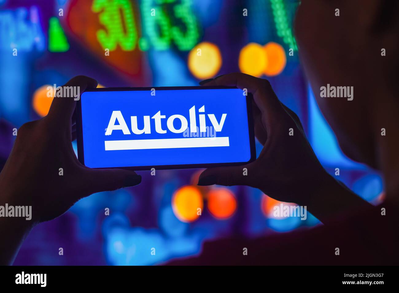 In this photo illustration, a silhouetted woman holds a smartphone with the Autoliv logo ...