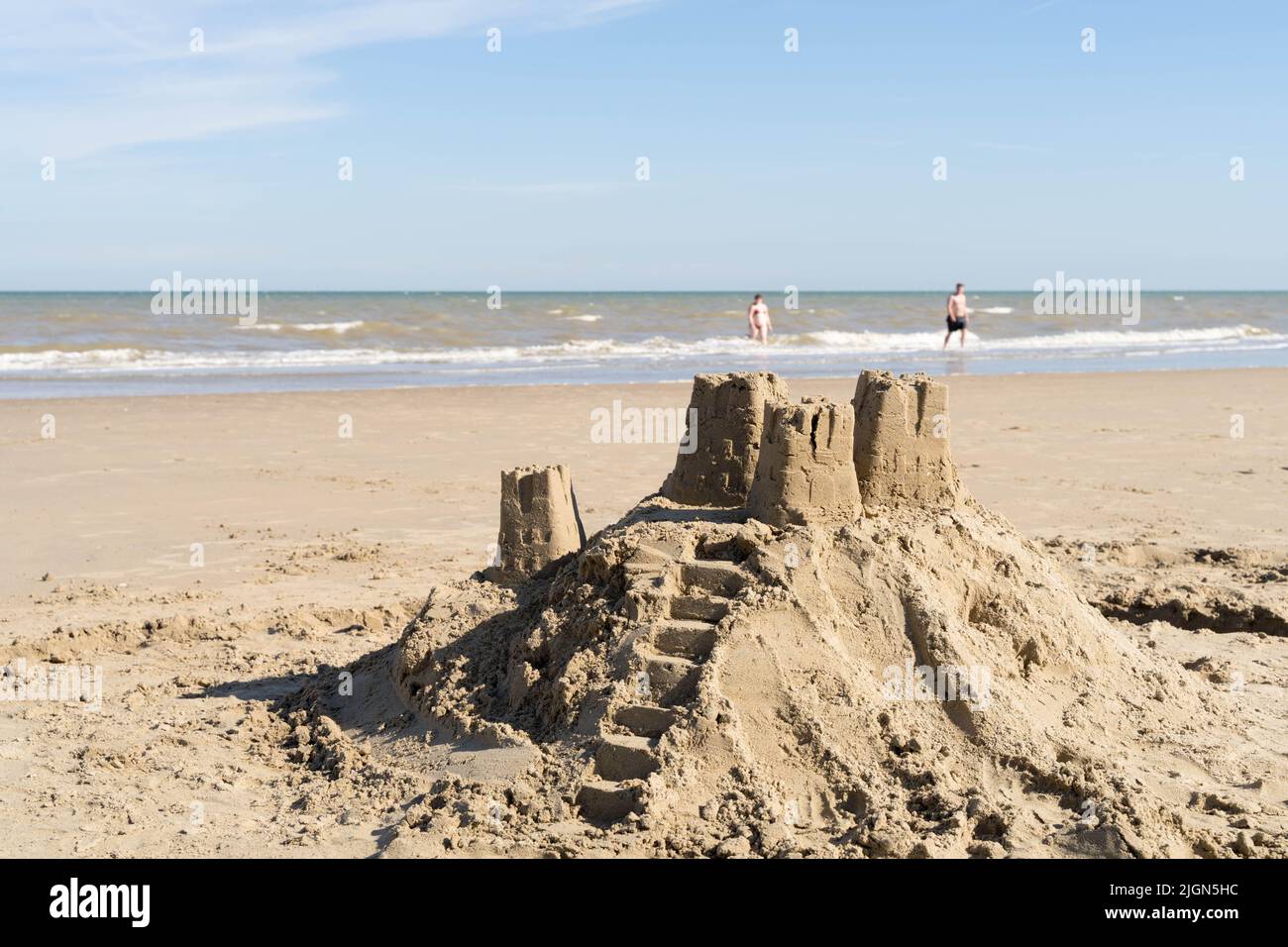 Sand castle built in sandy beach, with people playing with sea waves in ...