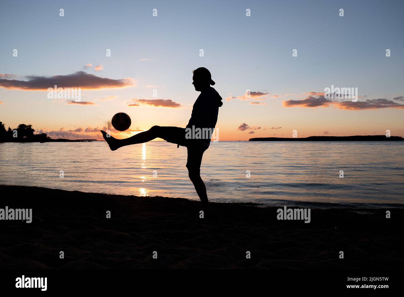 Man playing soccer on a beach at sunset. Dark evening view. Football ...