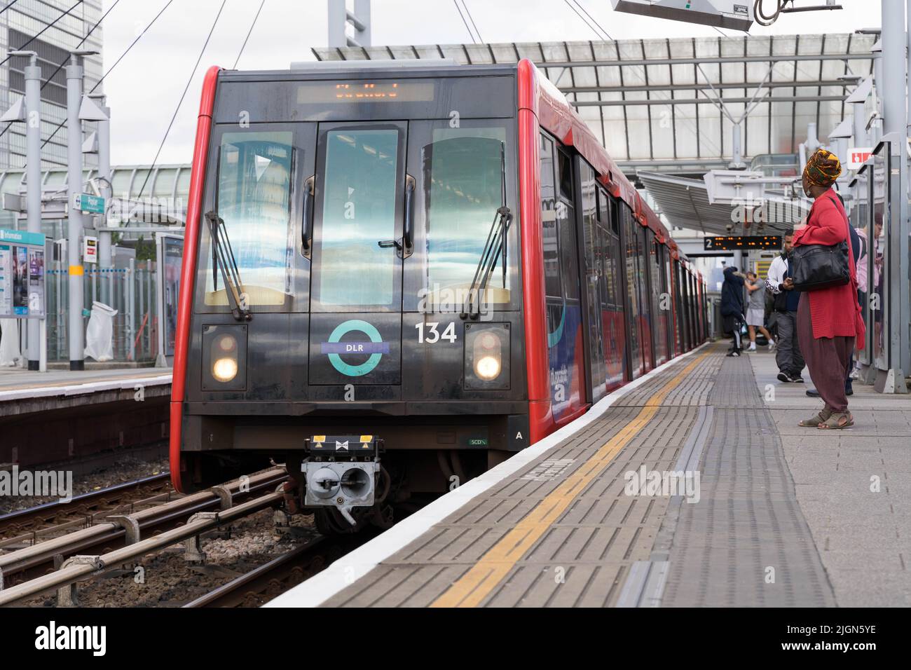 Woman in red passenger wait behind the yellow line on DLR train ...