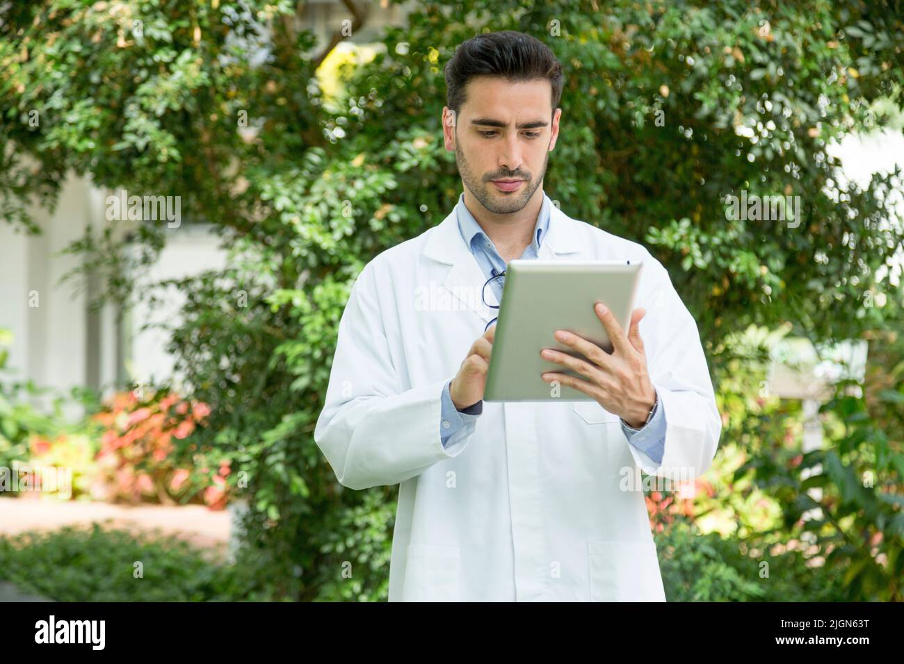 Portrait of a man in lab coat using a digital tablet standing in a ...