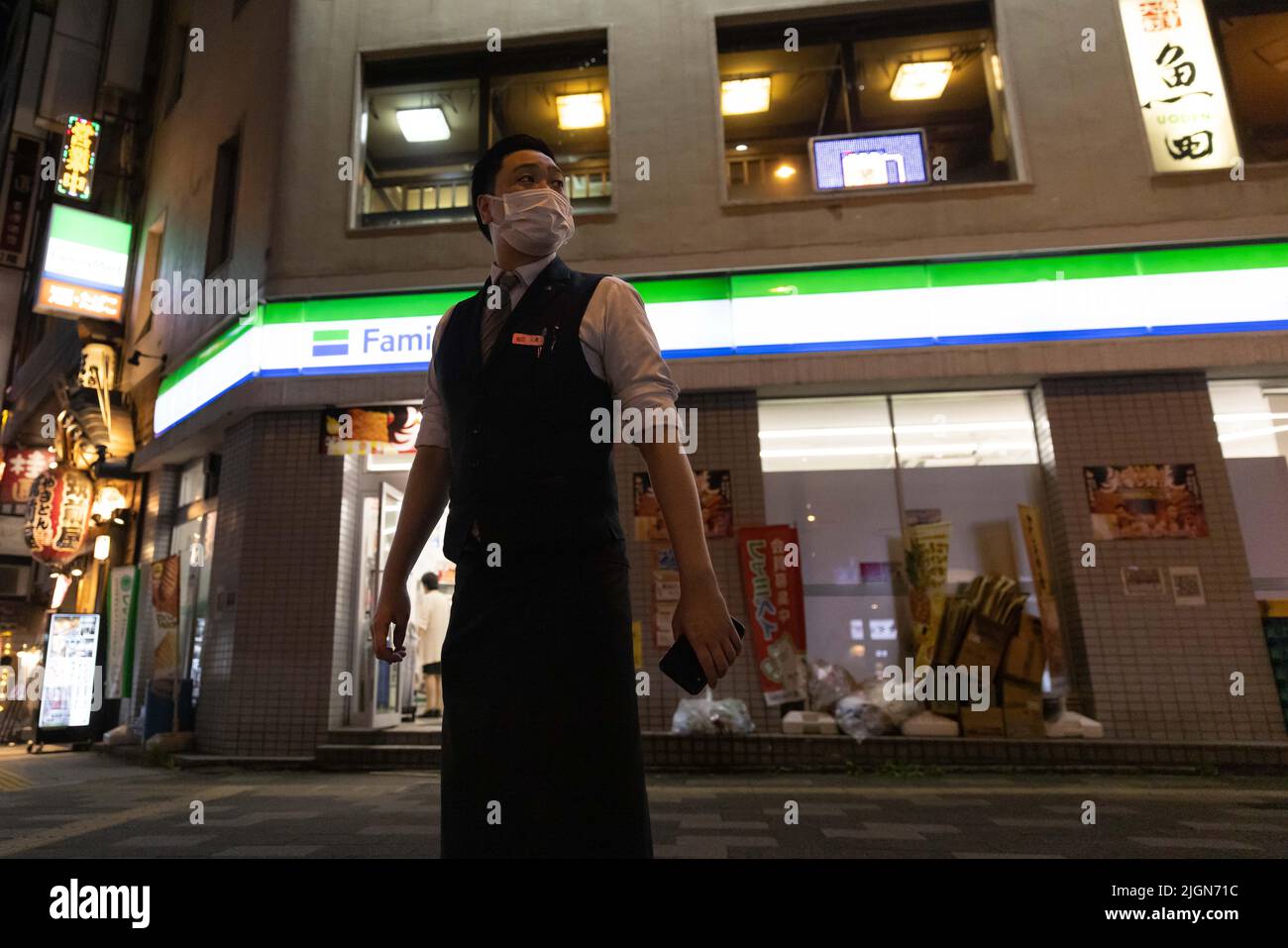 Restaurant employee stands in front of a FamilyMart convenience store ...