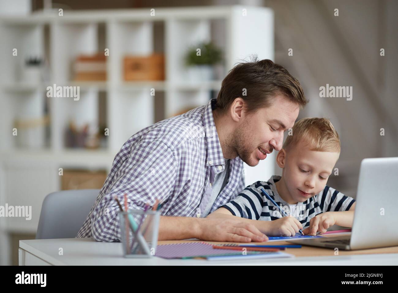 Smiling handsome young father in casual shirt sitting at table and ...