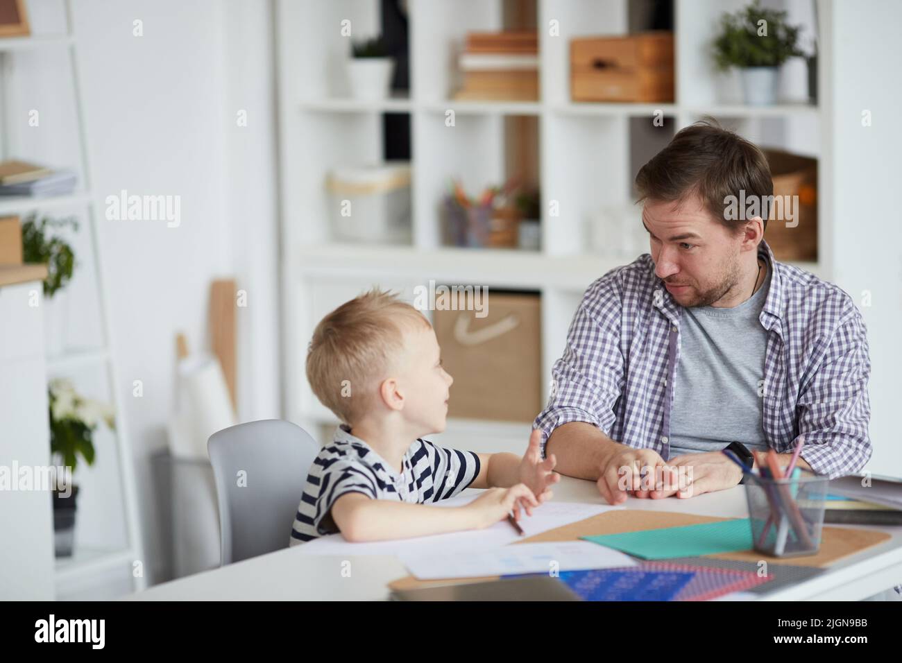 Surprised young father with frowning forehead sitting at table and ...