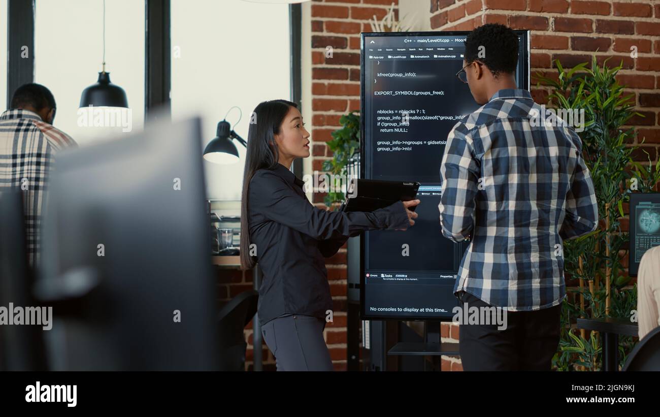 Team Of Coders Analyzing Code On Wall Screen Tv Comparing Errors Using Digital Tablet Next To