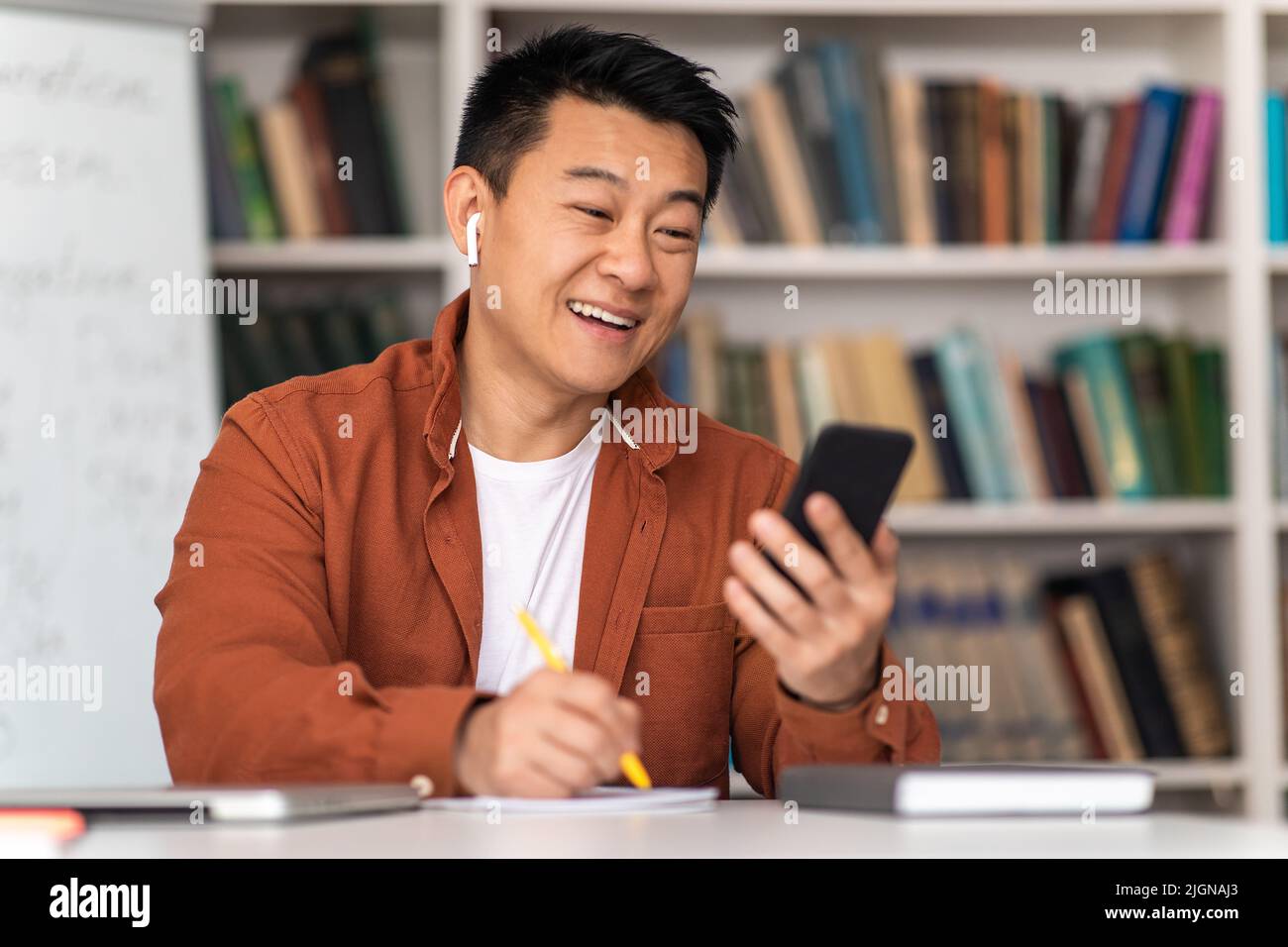 Asian Teacher Man Using Mobile Phone Wearing Earbuds In Classroom Stock ...