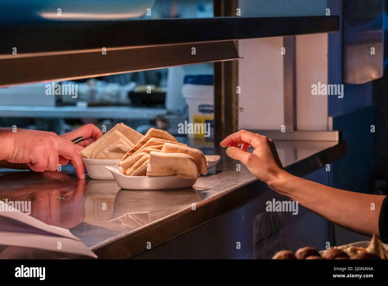 A volunteer collecting dishes of Flat Bread food at the pass to serve ...