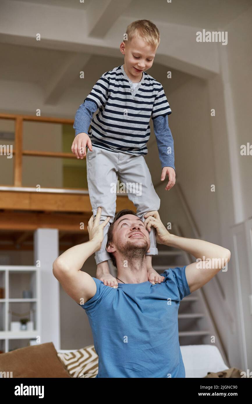 Smiling brave boy with blond hair standing on shoulders of father and ...