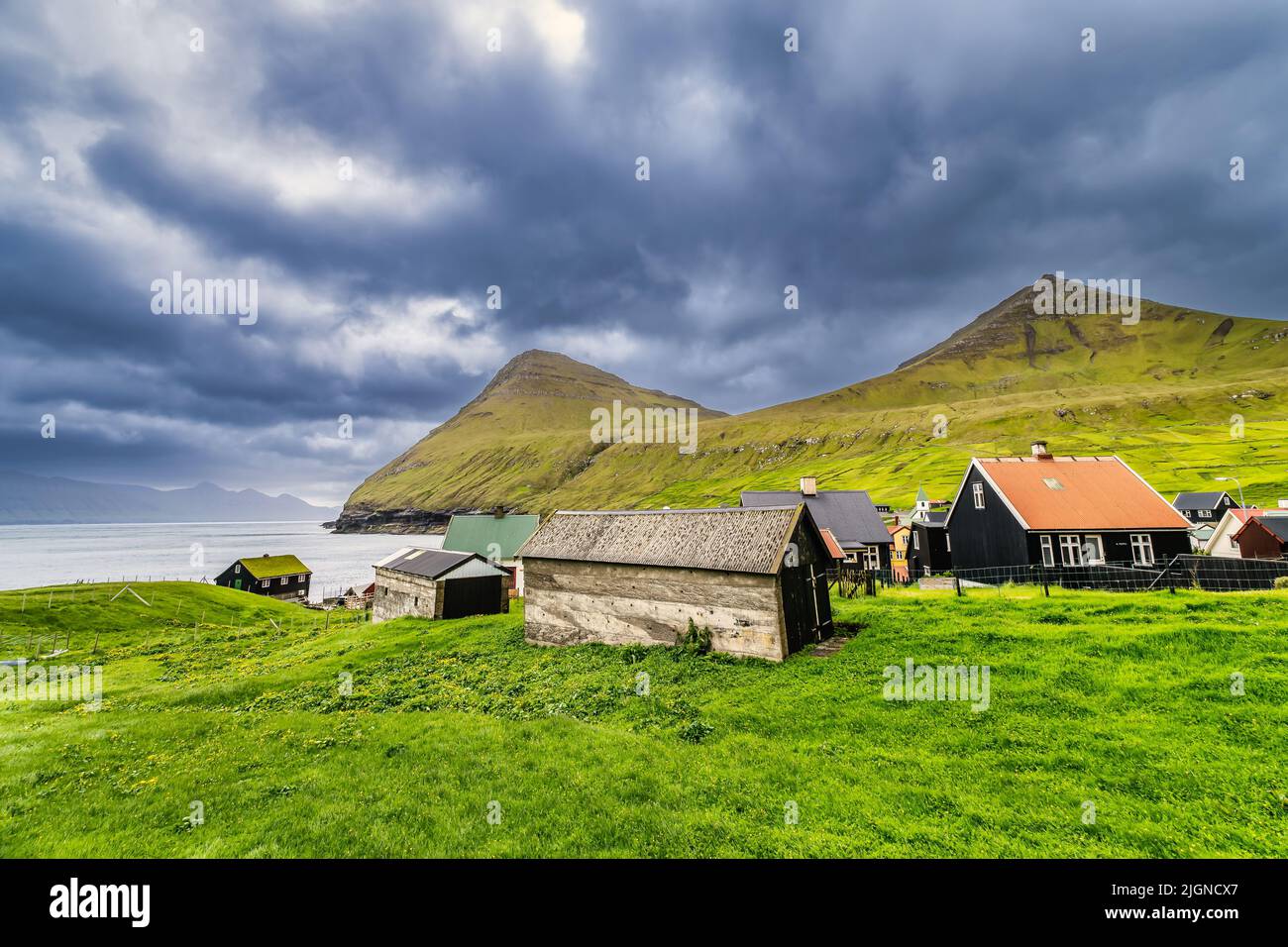 Colorful houses of Gjogv village and a small river flows into fjord ...
